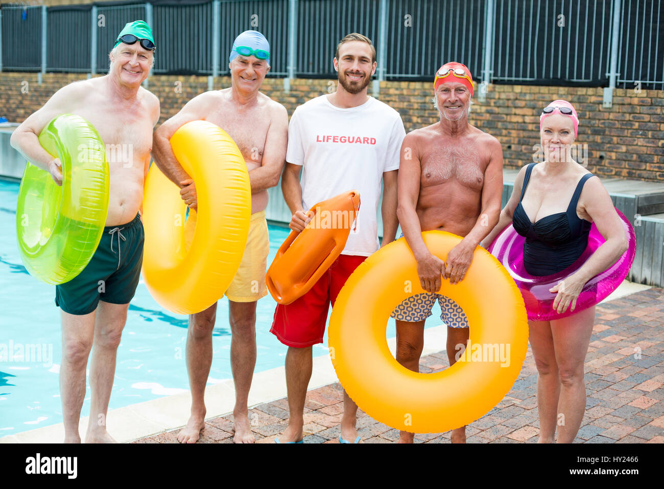 Portrait of male lifeguard with senior swimmers standing at poolside ...