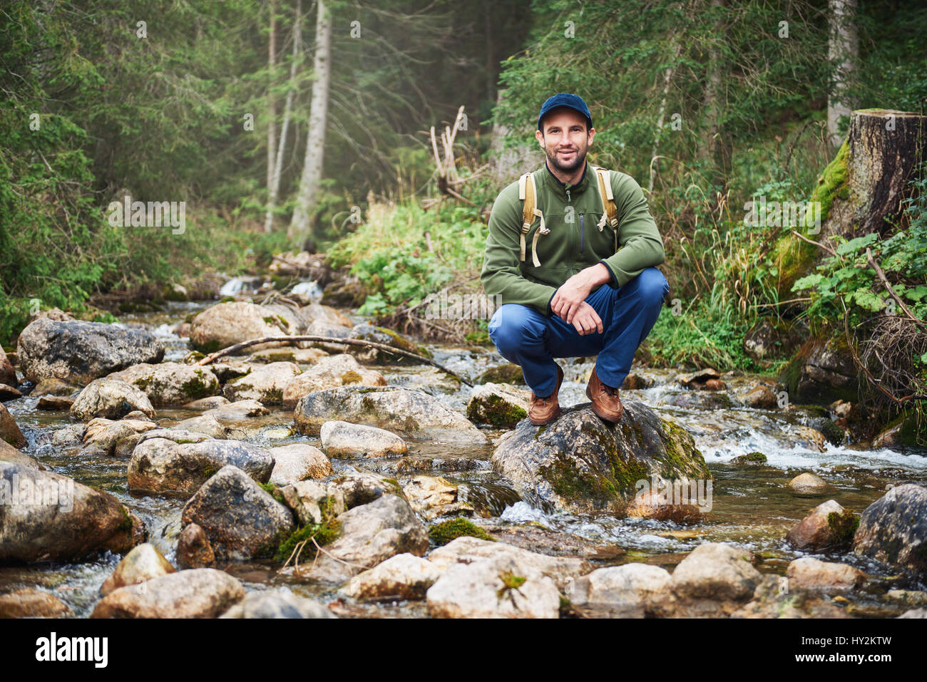 Young hiker crouching by a river in the woods Stock Photo - Alamy