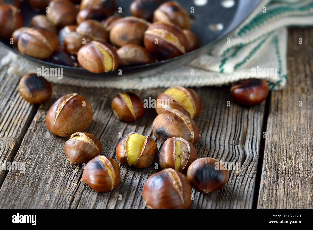 Roasted chestnuts with a perforated chestnut pan on an old wooden table ...