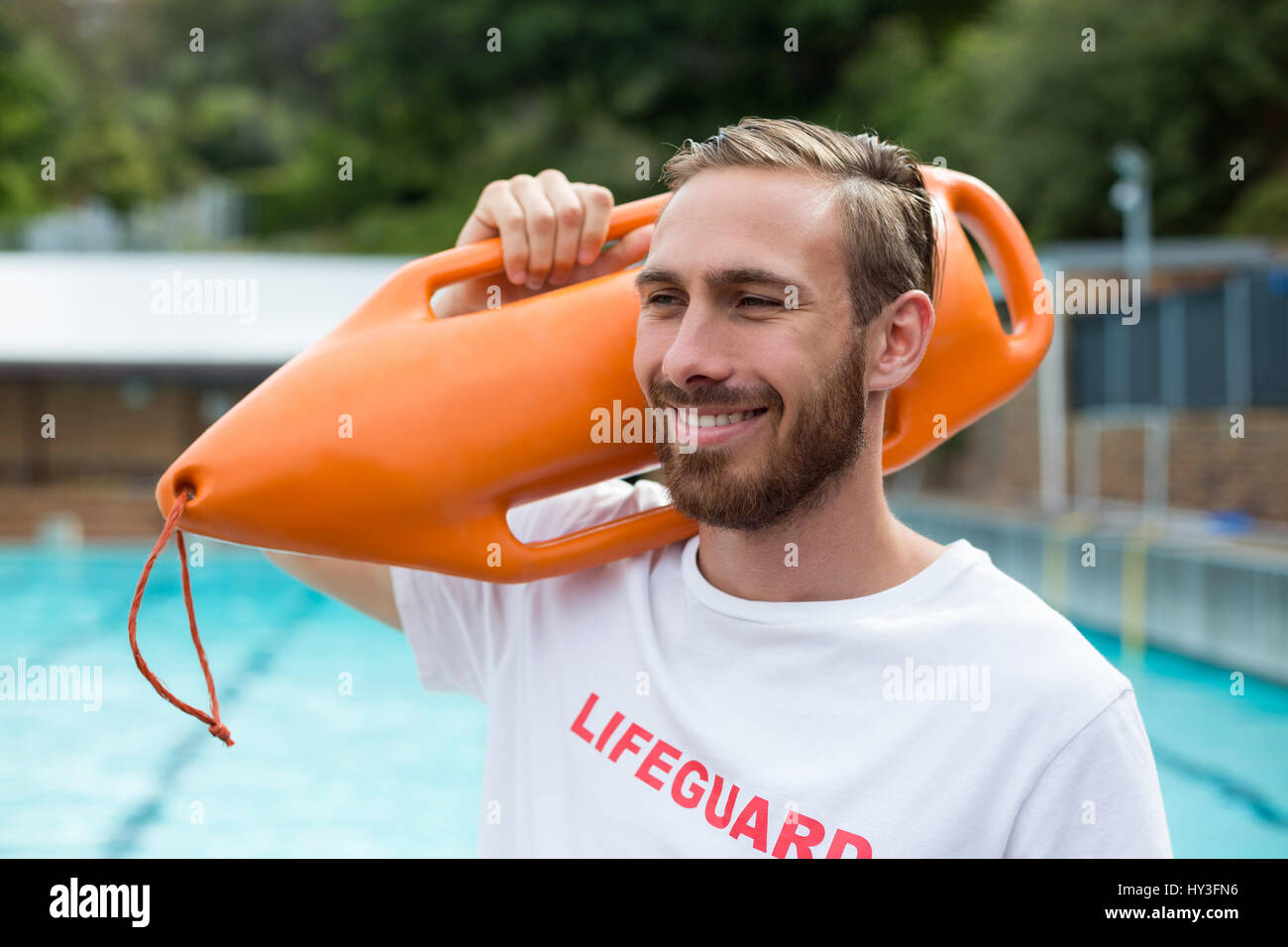 Close up of smiling male lifeguard carrying rescue can at poolside ...
