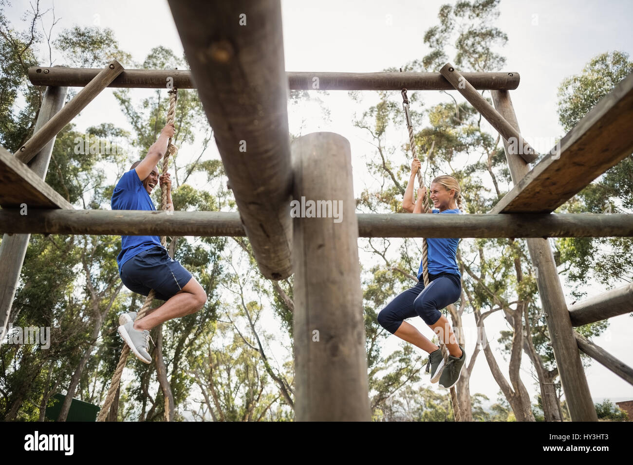 Fit man and woman climbing rope during obstacle course in boot camp ...