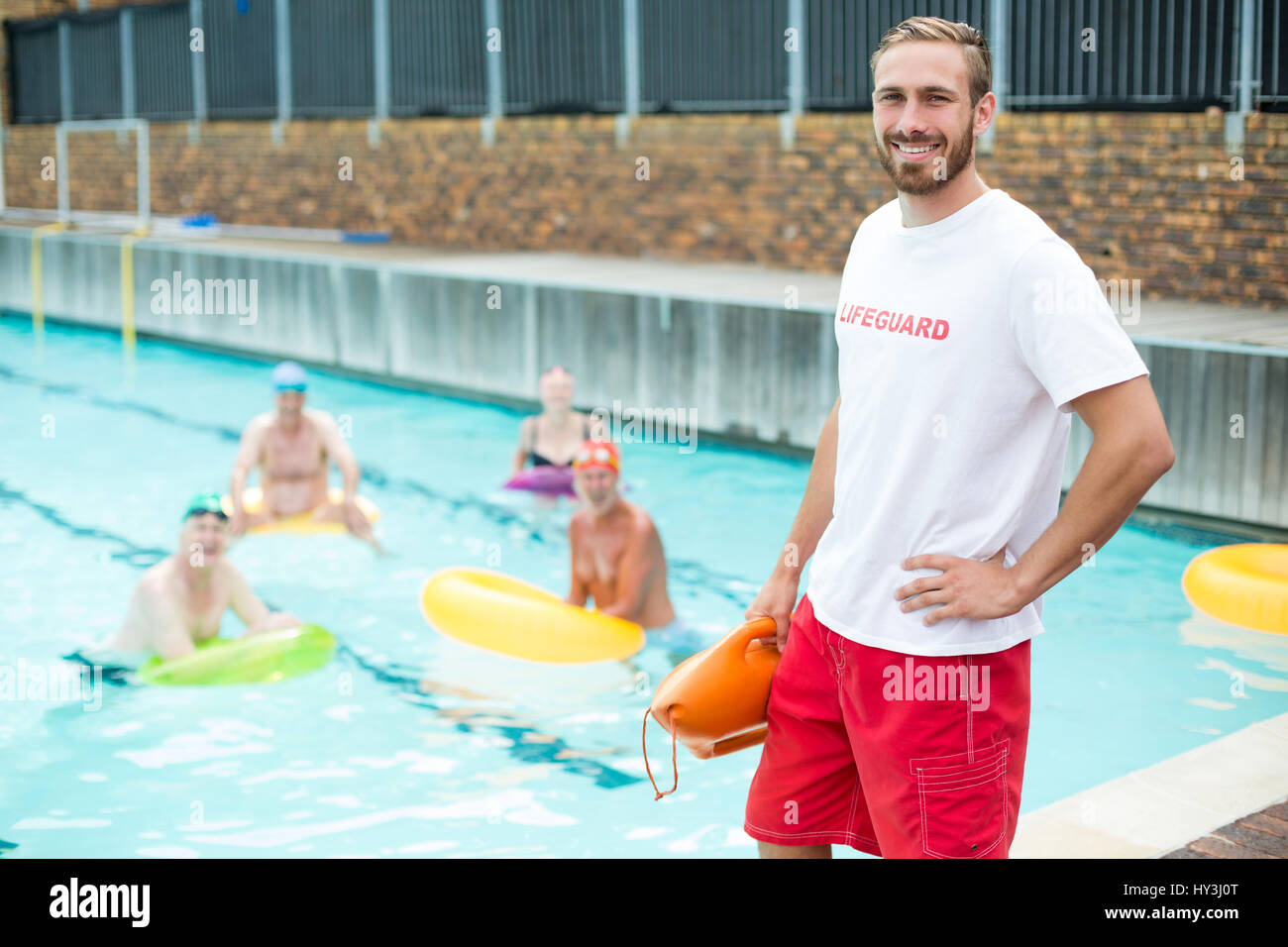 Portrait of male lifeguard standing while swimmers swimming in pool ...