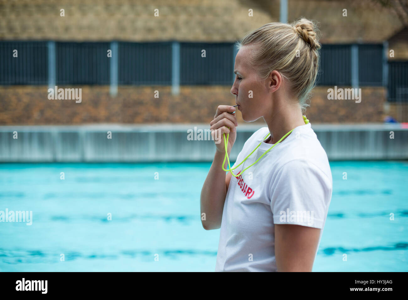 Side view of female lifeguard whistling at poolside Stock Photo - Alamy