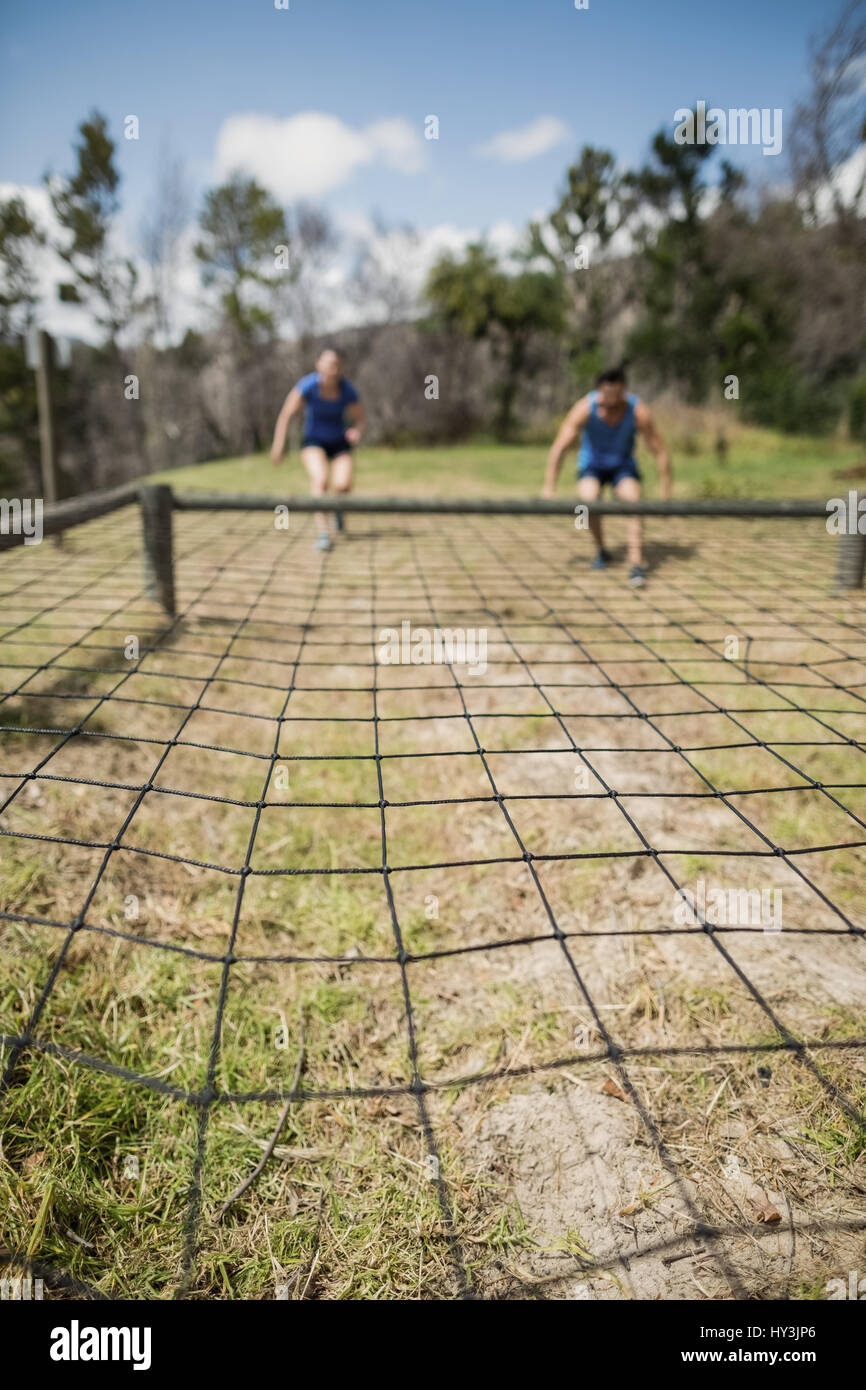 Fit man and woman crawling under the net during obstacle course in boot ...