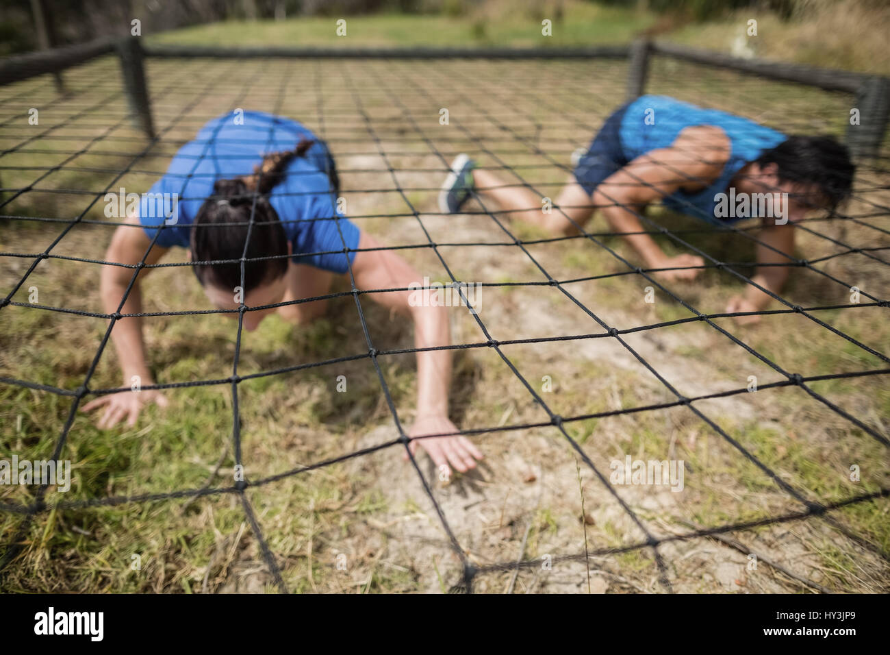 Fit man and woman crawling under the net during obstacle course in boot ...