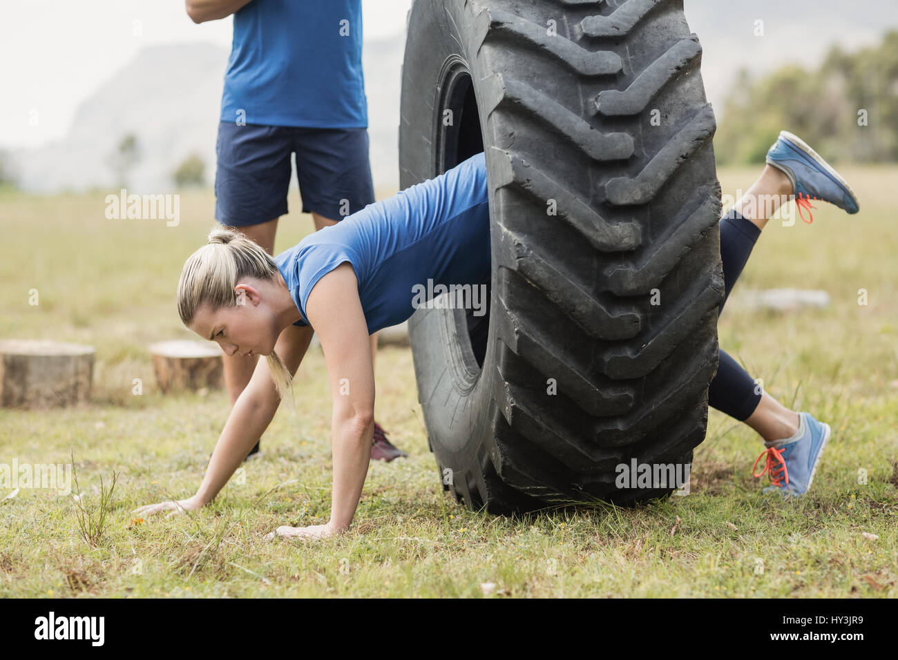 Woman crawling through the tire during obstacle course in boot camp ...