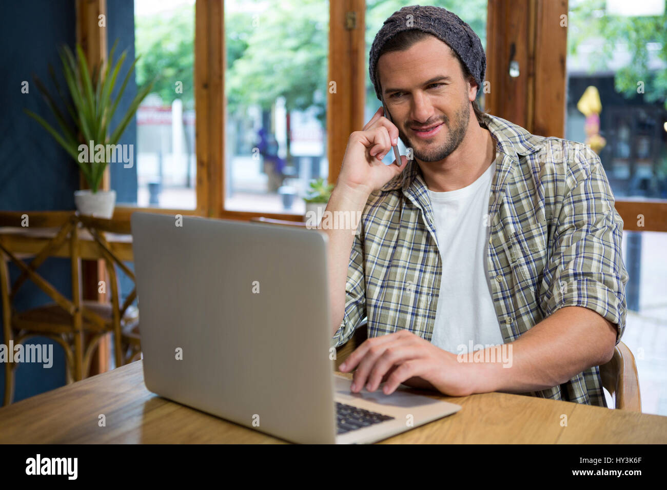 Handsome young man talking on phone while using laptop in coffee shop ...
