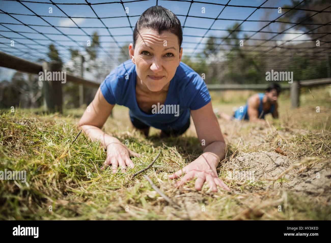 Fit woman crawling under the net during obstacle course in boot camp ...