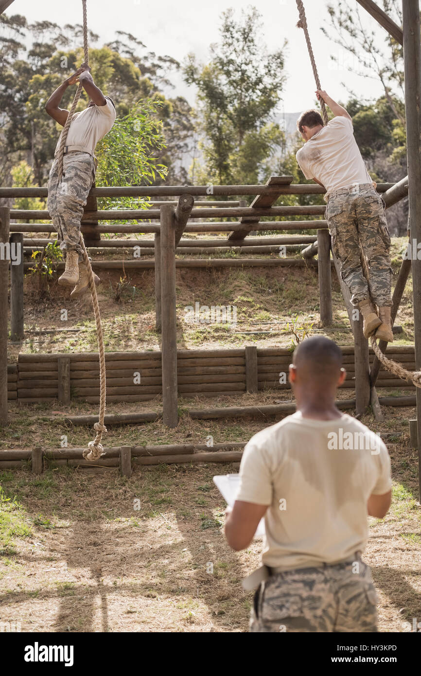 Military soldiers climbing rope during obstacle course training at boot ...