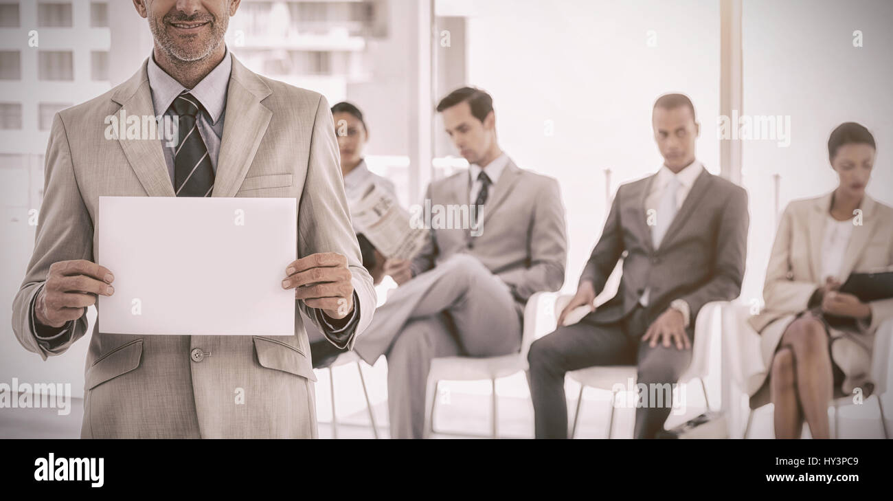 Smiling businessman holding blank notice with people waiting behind ...