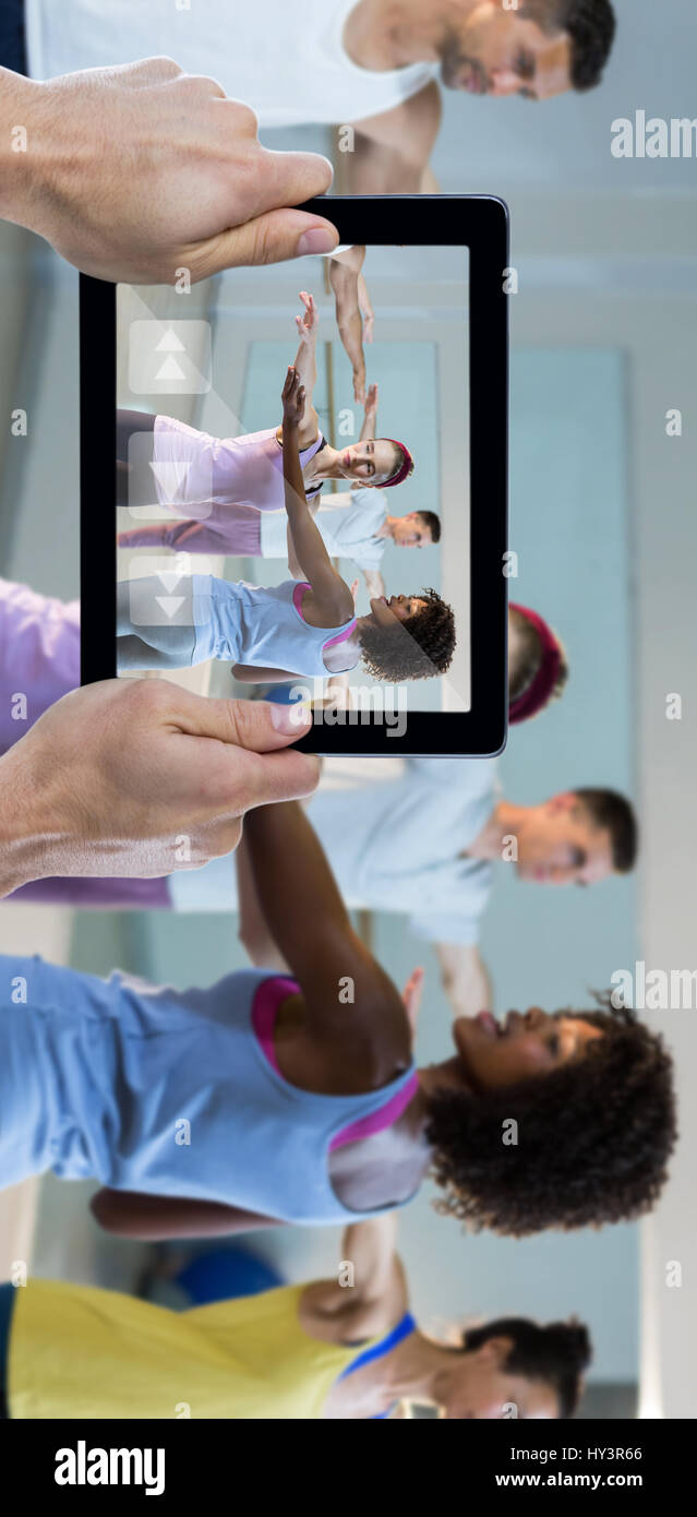 Cropped hand holding digital tablet against yoga instructor helping ...