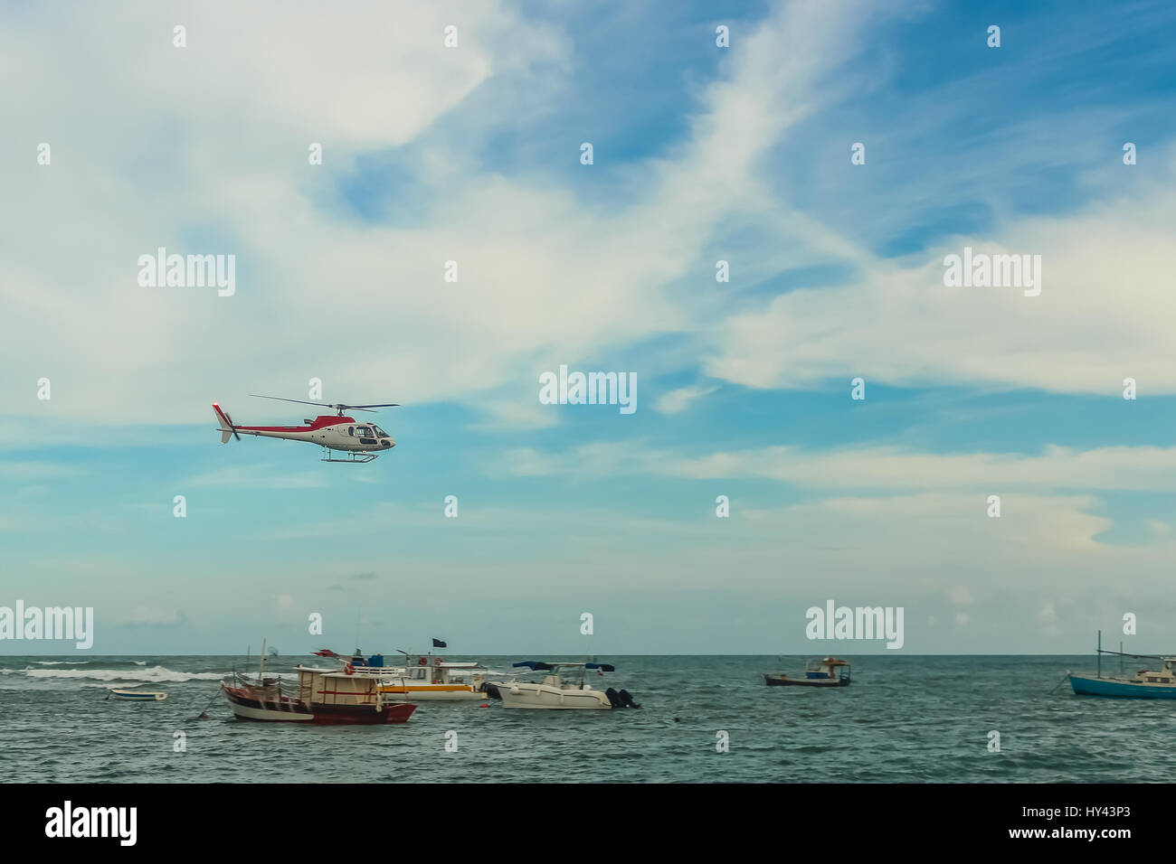 Helicopter flying in a blue sky with puffy clouds over the sea full of ...