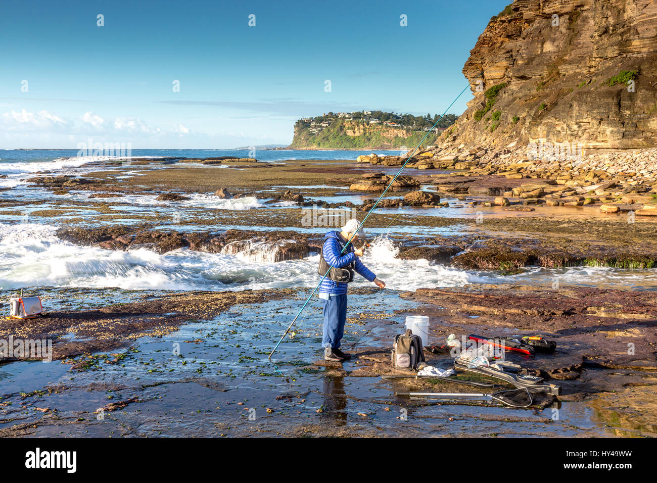 Asian man Rock fishing at Bilgola beach in Australia, wearing a life ...