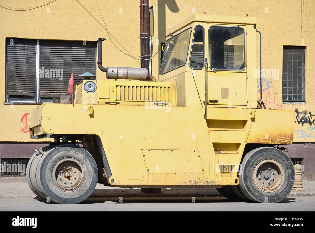 Yellow roller on the street parked near a building Stock Photo - Alamy