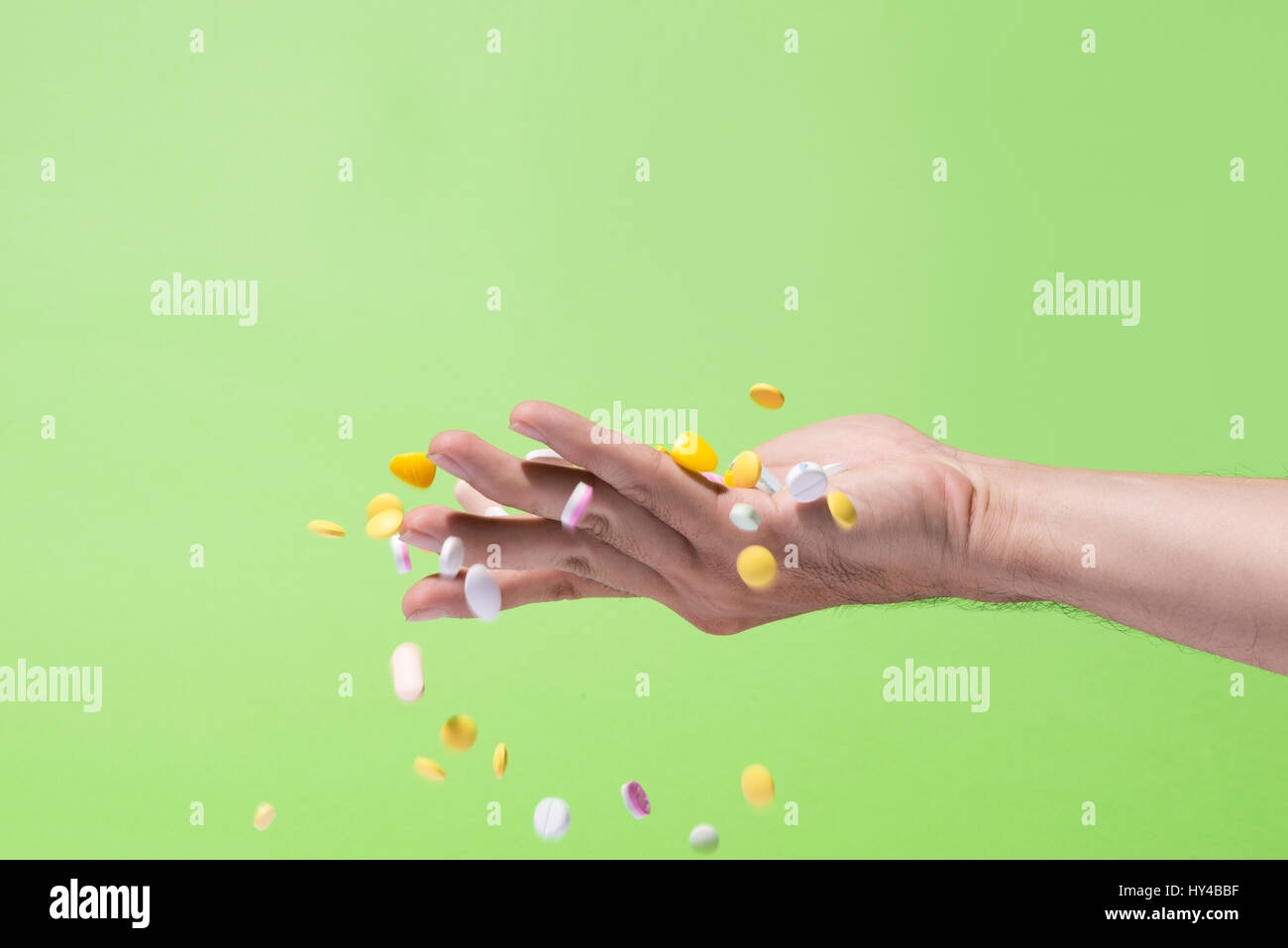 Colored pills falling from hand on green background Stock Photo - Alamy