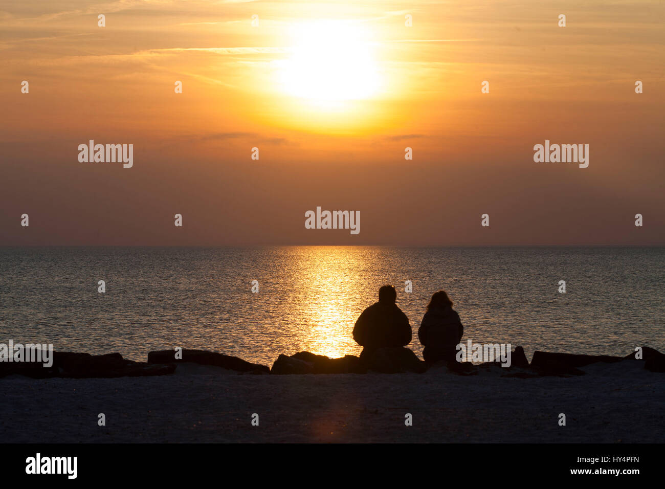 Couple watching sunset on the beach Stock Photo - Alamy