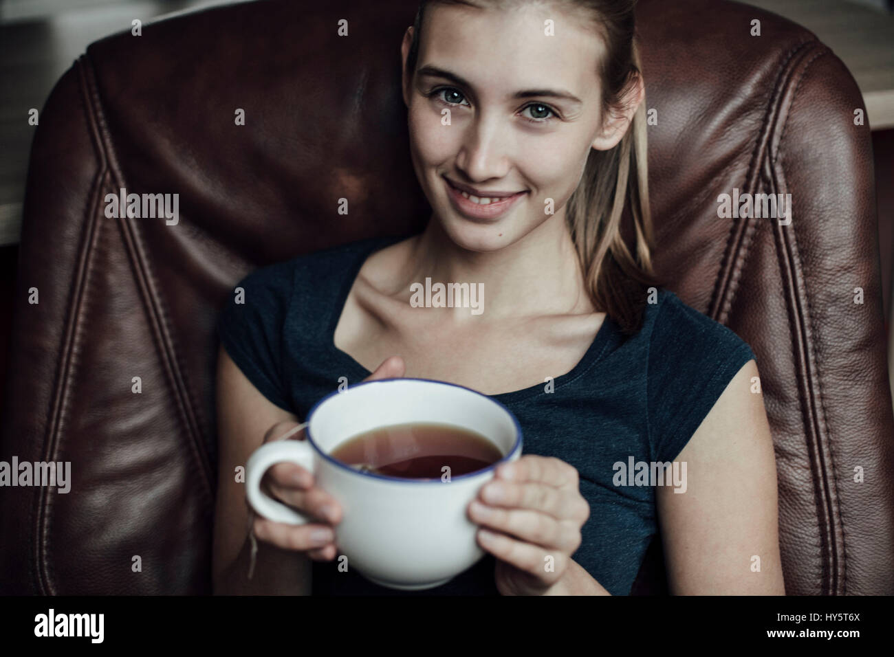 Young woman sitting in armchair and drinking tea Stock Photo - Alamy