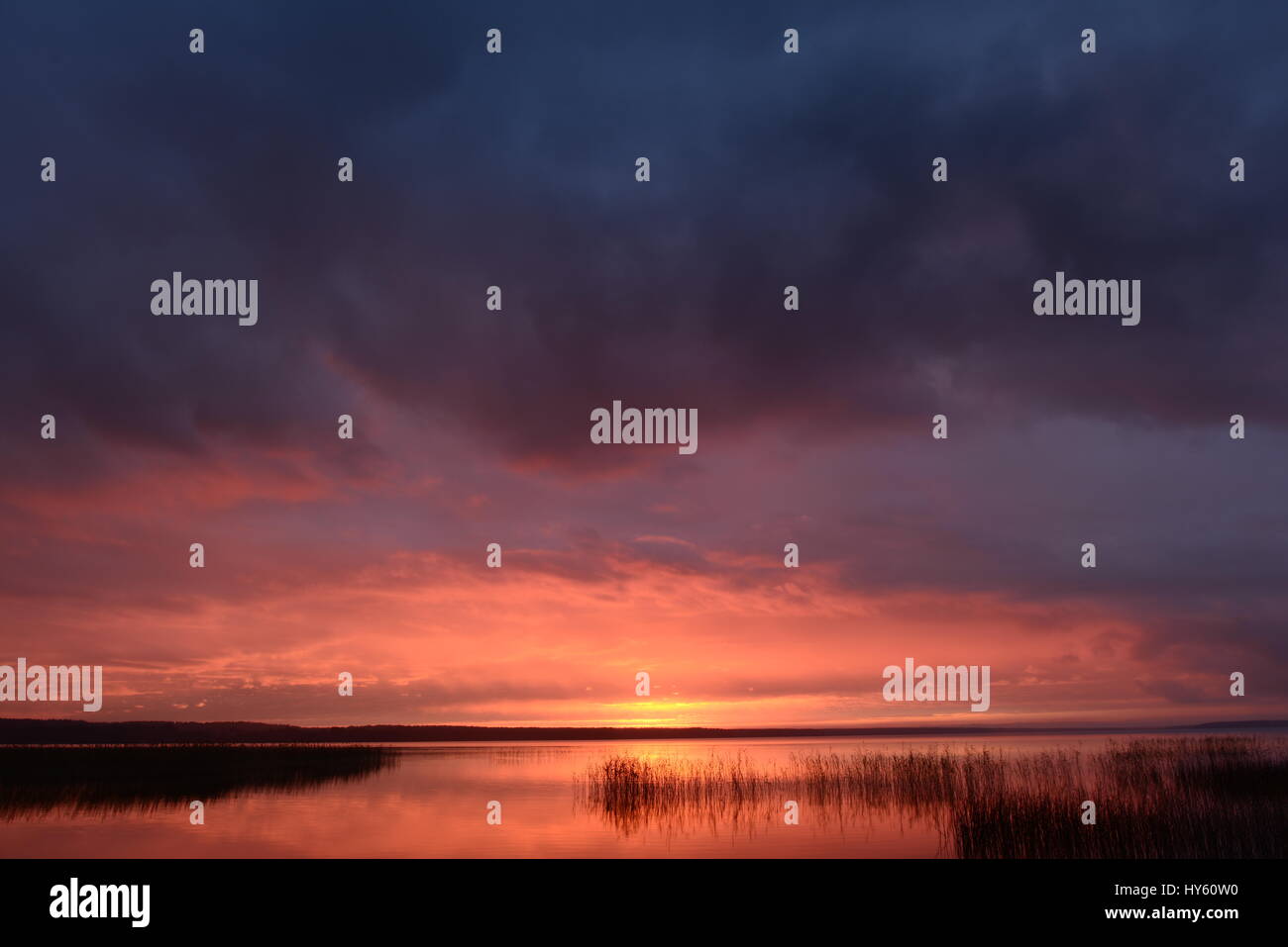 Gloomy sunset in the cloudy sky above the surface of the lake water ...