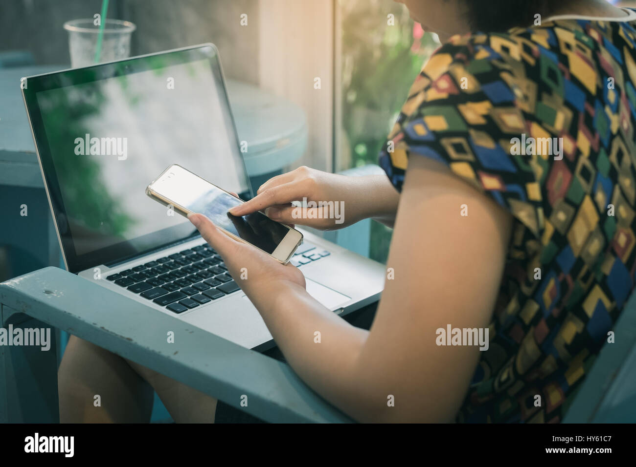 Asian woman using smartphone at home while working with laptop computer ...