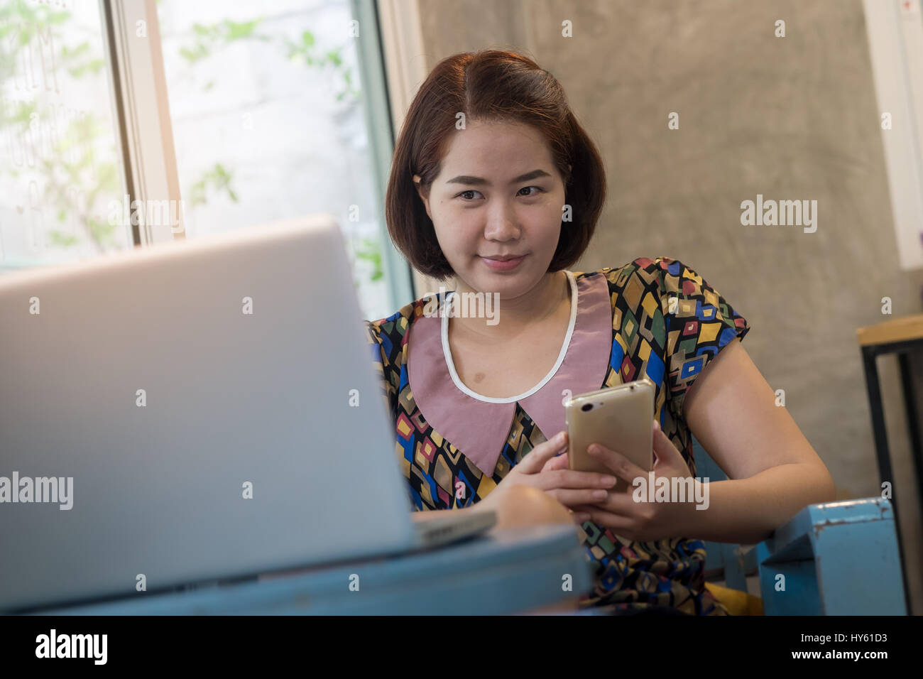 Asian woman using smartphone at home while working with laptop computer ...