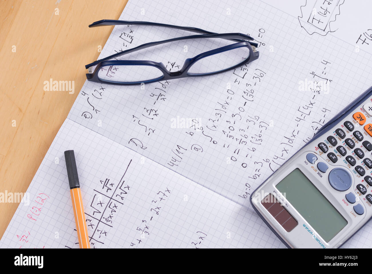 A desk with an exercise book, glasses, pens and a calculator for ...