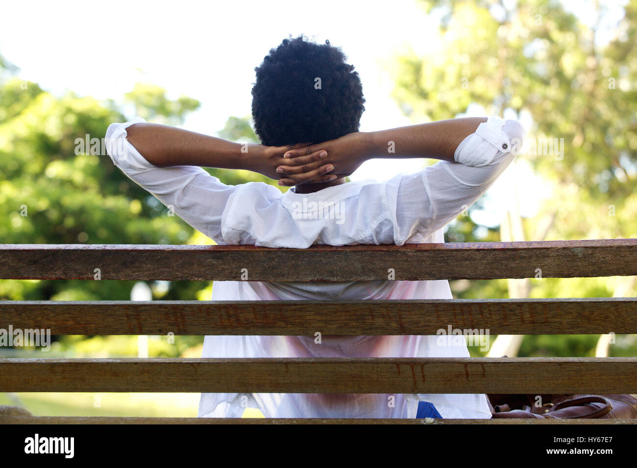 Rear portrait of young woman relaxing on park bench with hands behind ...
