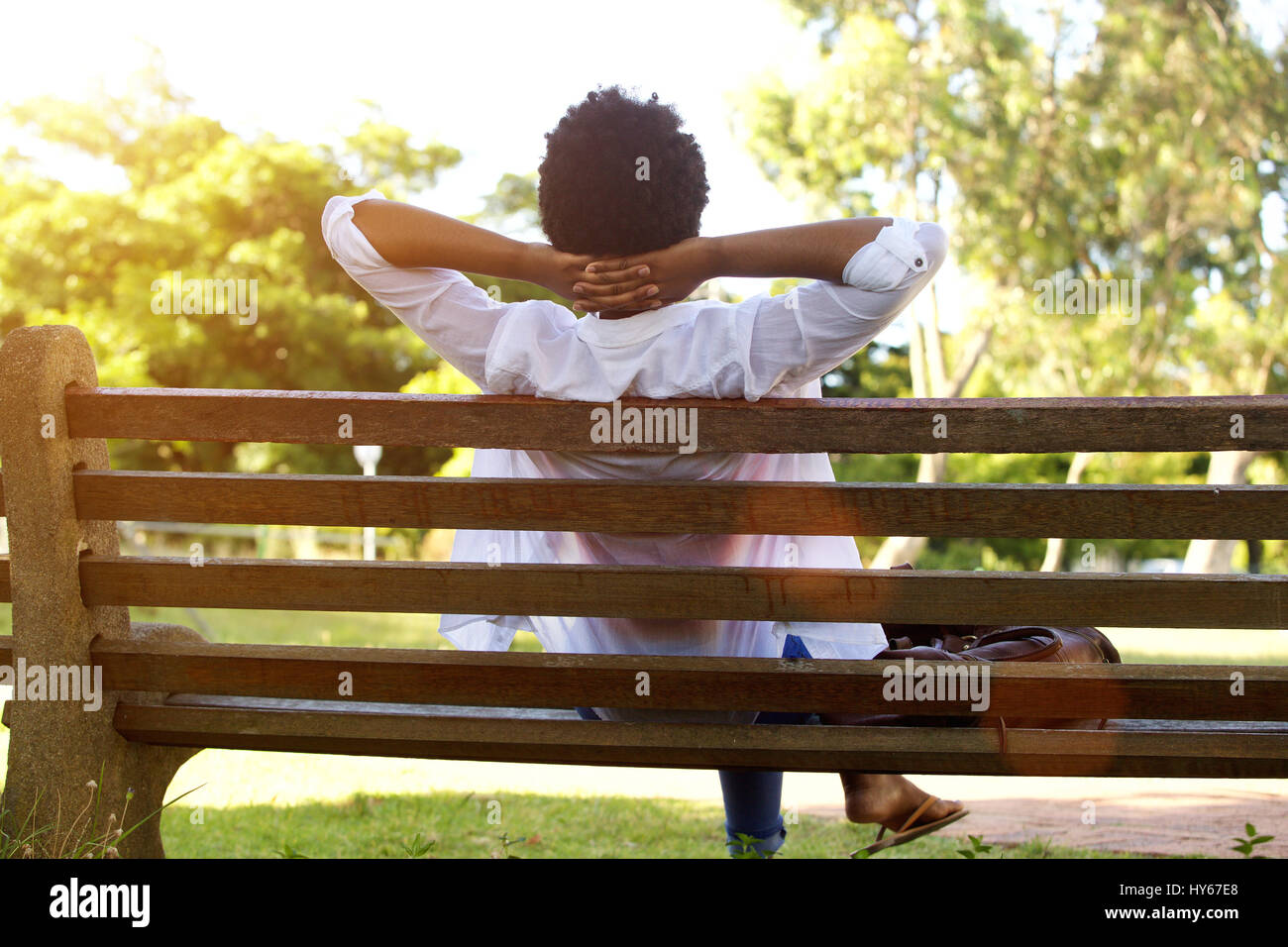 Rear portrait of young lady sitting relaxed on a park bench with hands ...