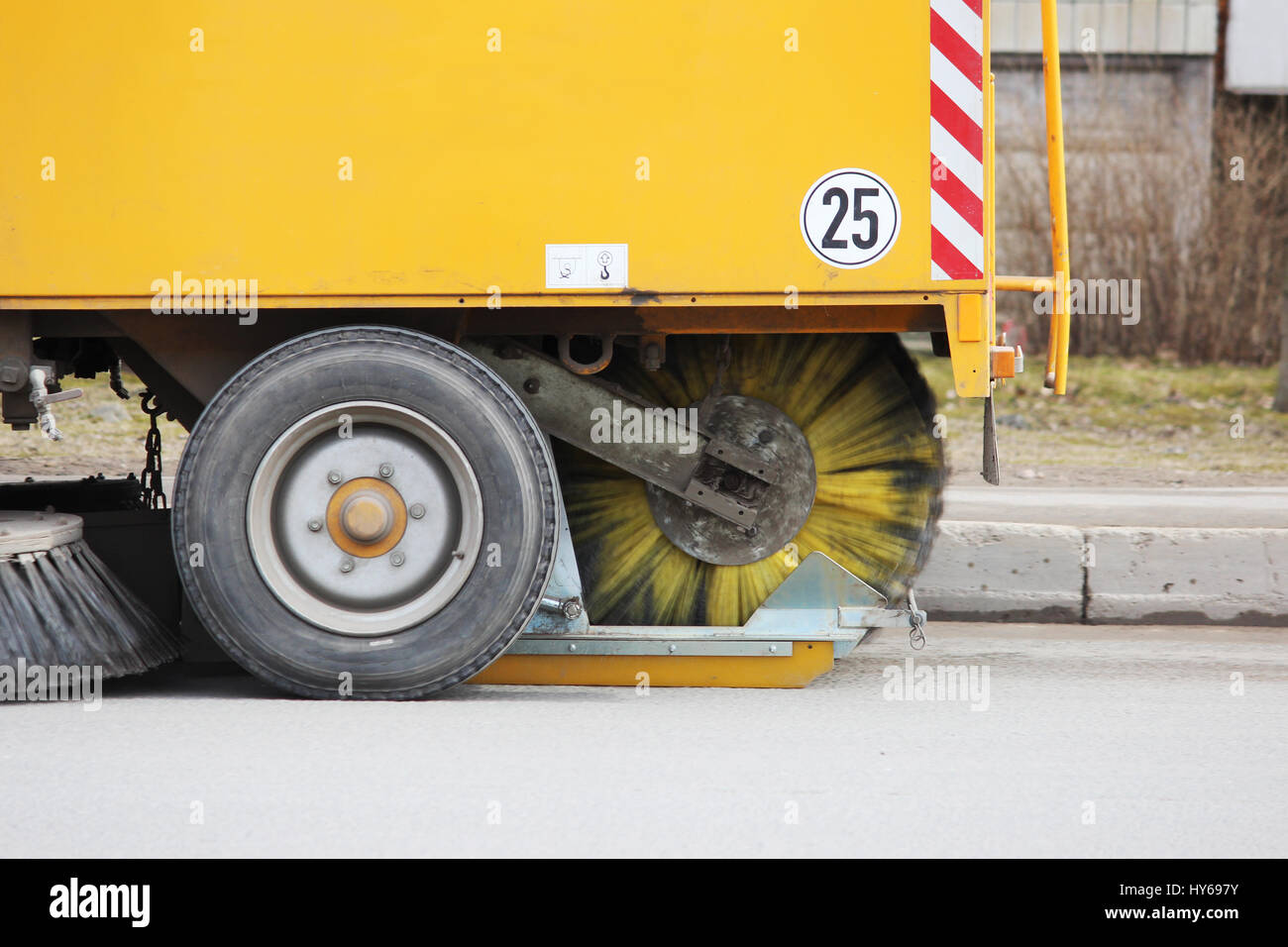 Yellow urban sweeper cleans road from dirt with a round brush in the ...