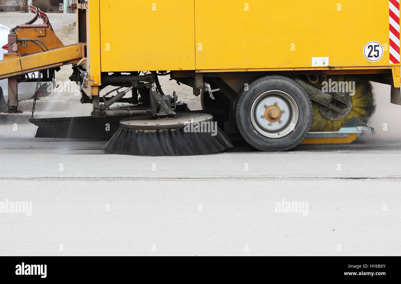 Yellow urban sweeper cleans road from dirt with a round brush in the ...