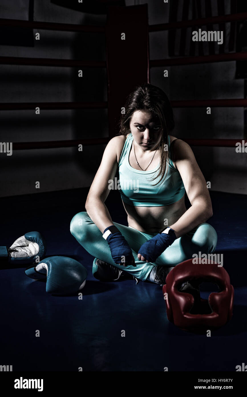 Female boxer sitting near lying boxing gloves and helmet in regular ...