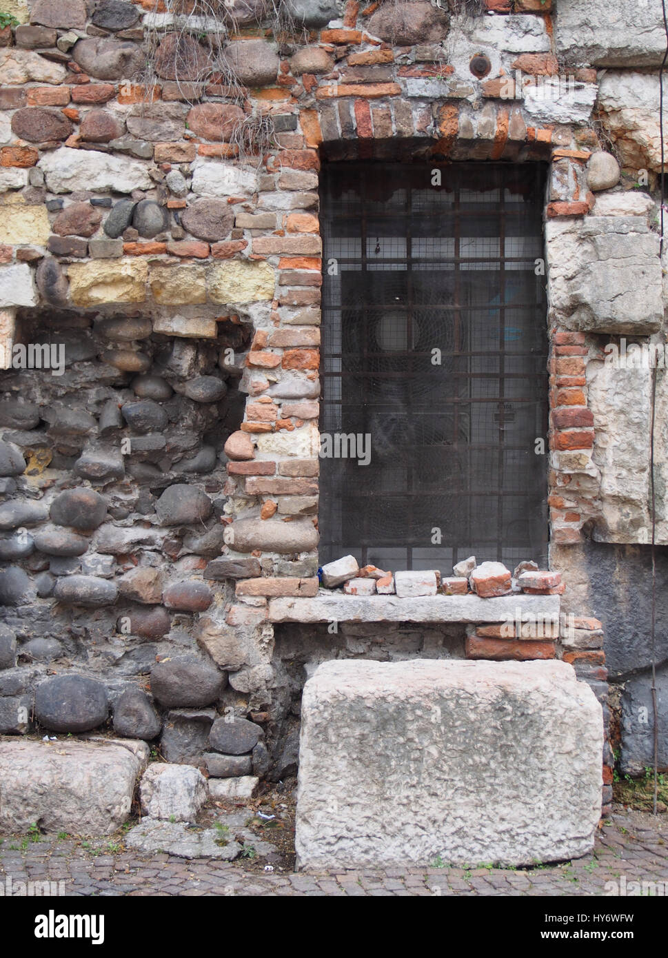 oldamaged and repaired brick wall with a barred window and old stones ...