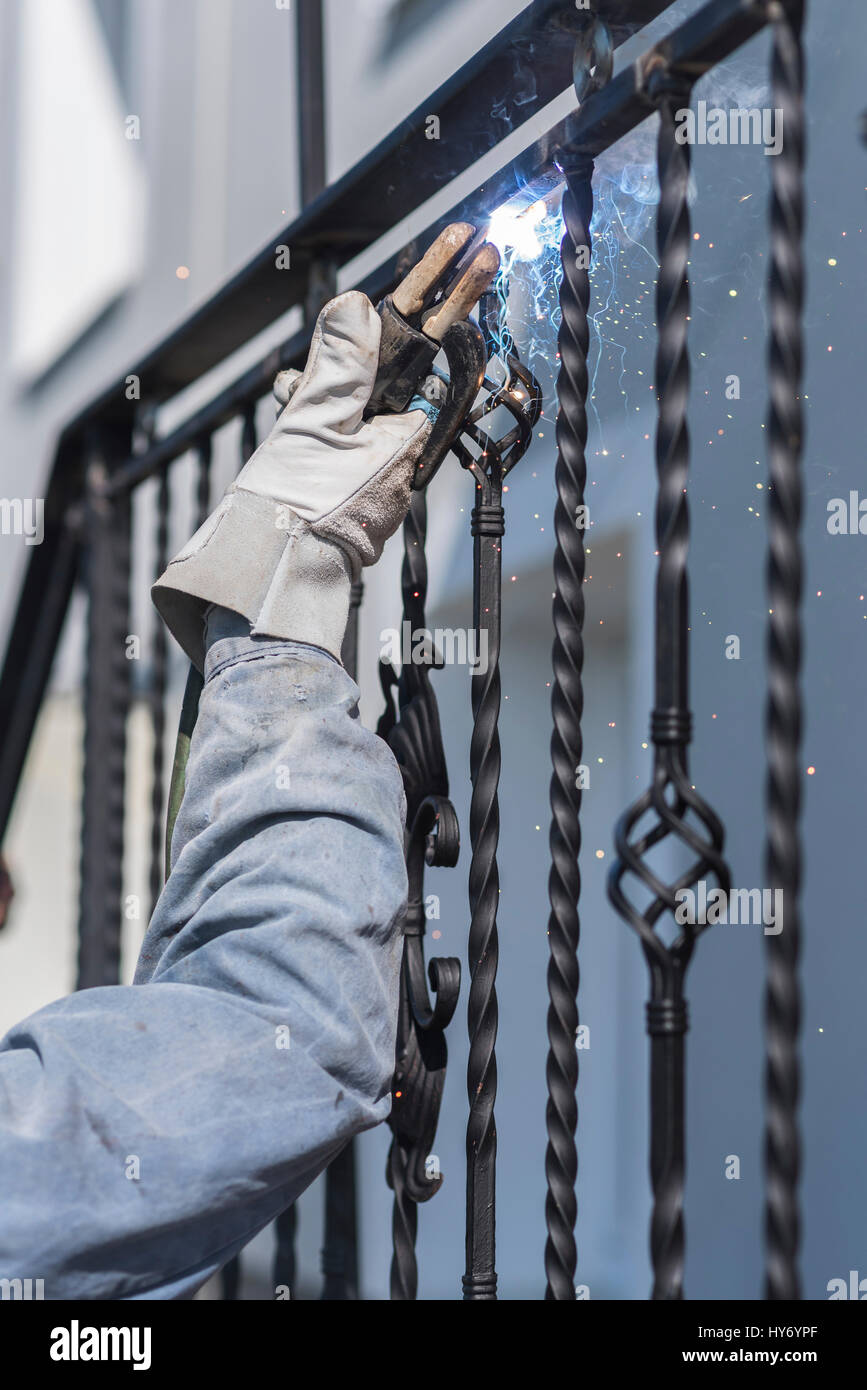 A worker welding metal handrails on the stairs. Wrought iron railings ...