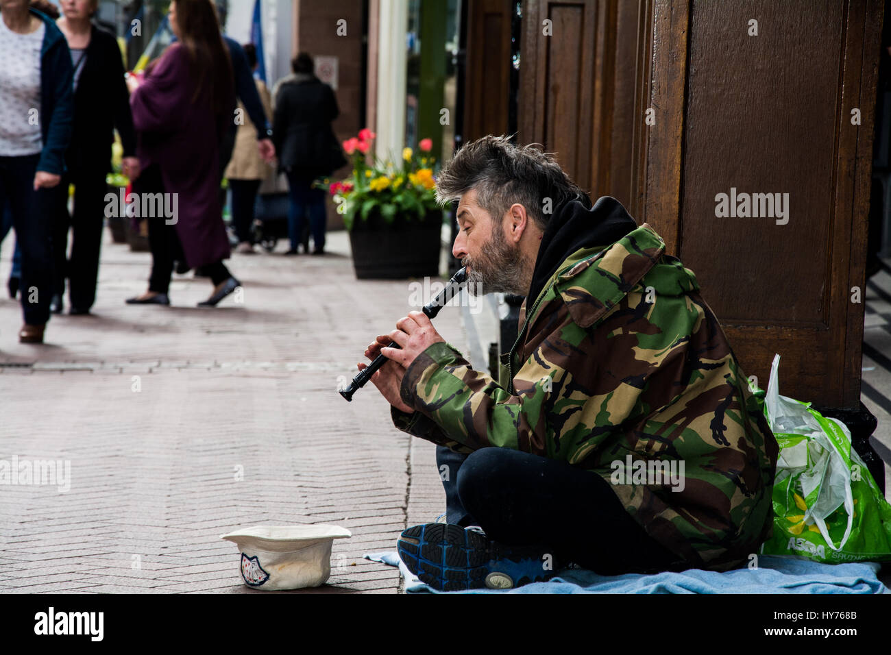 A homeless man busking in Shrewsbury town centre. Playing a recorder ...