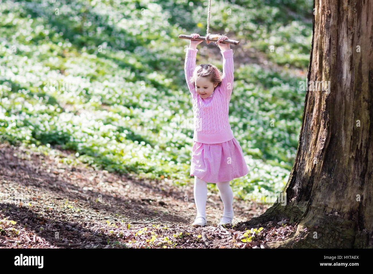Cute Little Girl In Pink Dress On Tree Rope Swing In Blooming Spring cute-little-girl-in-pink-dress-on-tree-rope-swing-in-blooming-spring