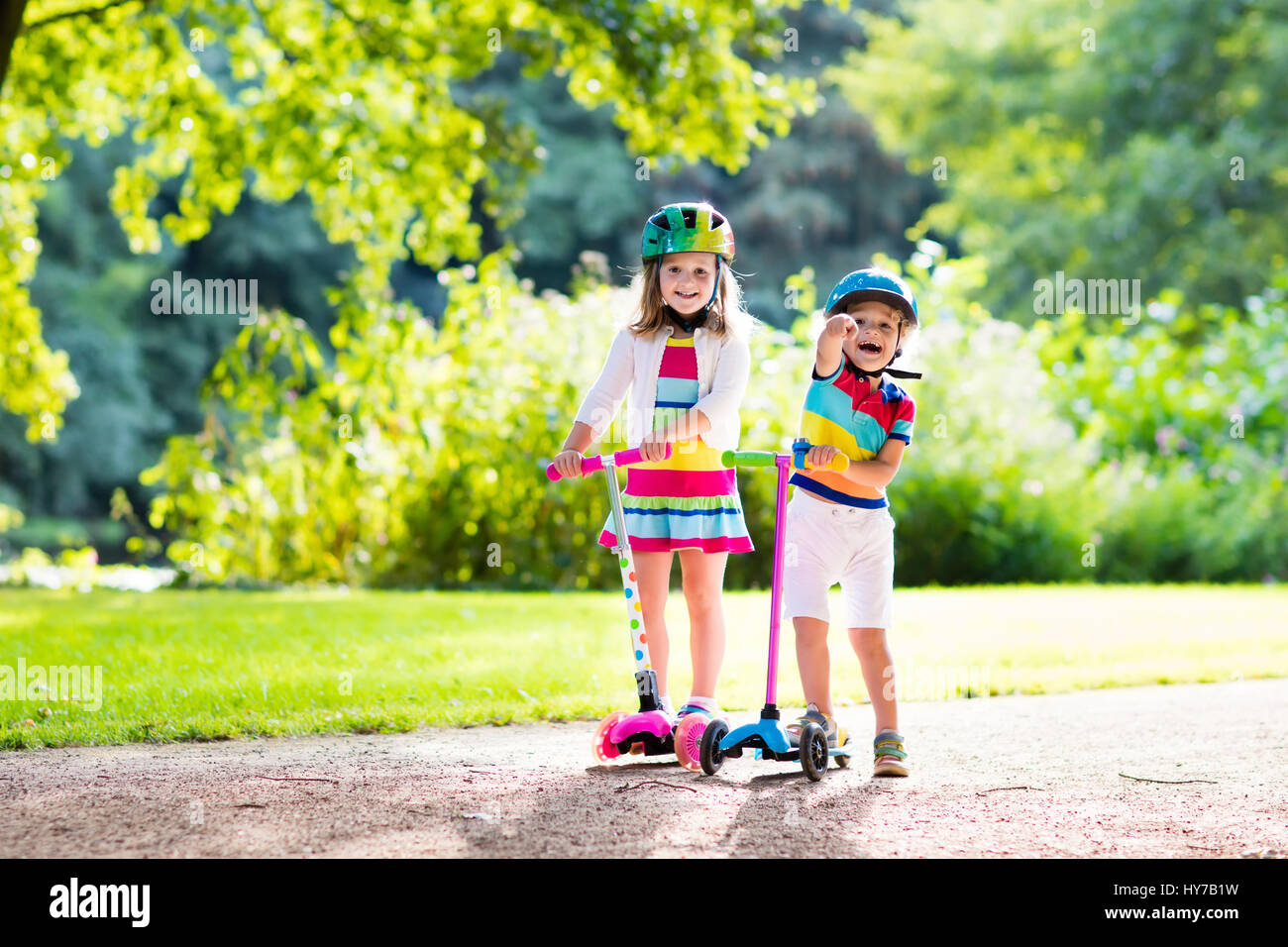 Children learn to ride scooter in a park on sunny summer day ...