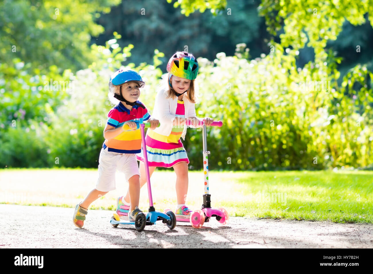 Children learn to ride scooter in a park on sunny summer day ...