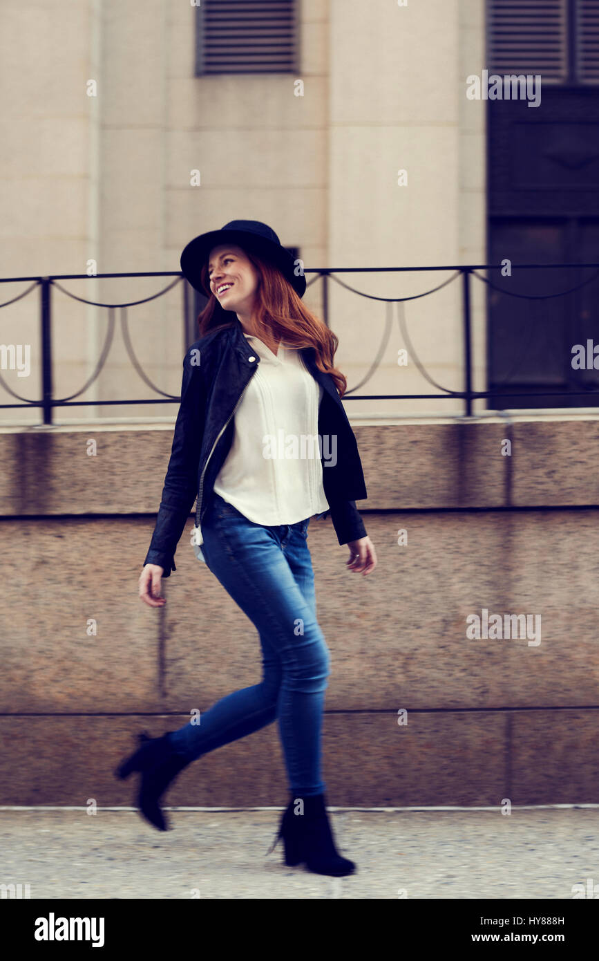 Young women in jeans and hat walking by railings in New York street ...