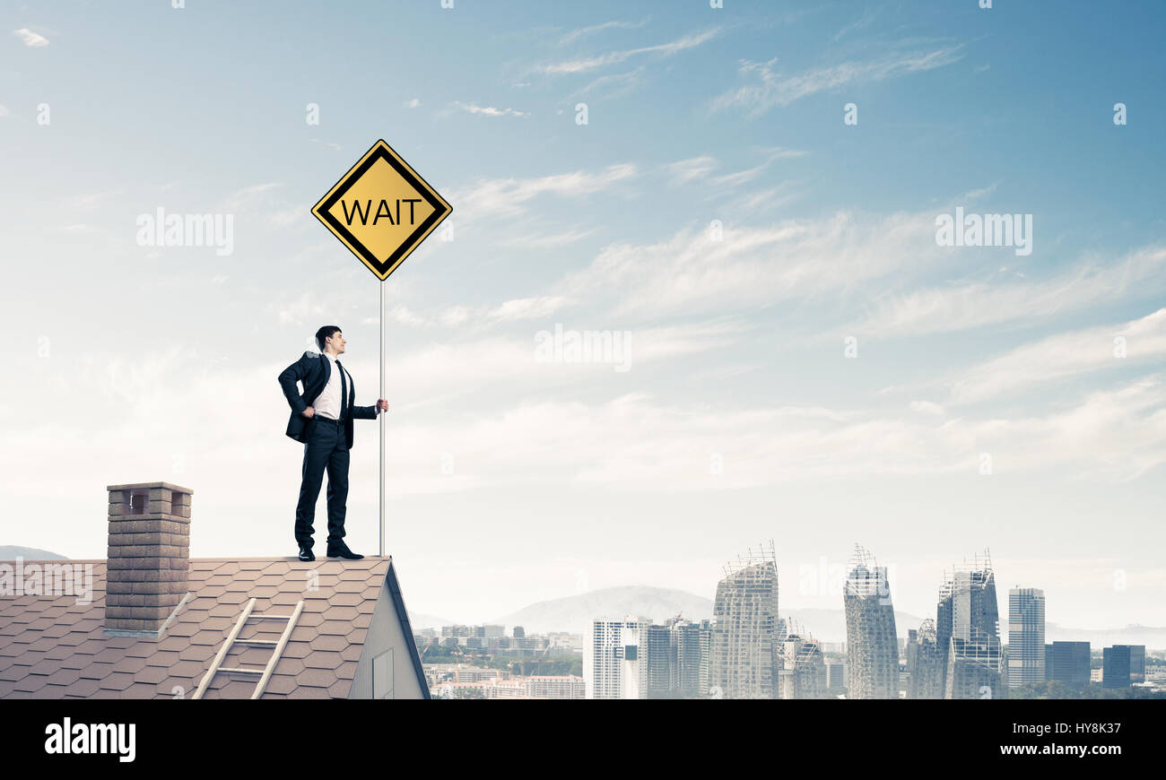 Young businessman on house brick roof holding yellow signboard a Stock ...