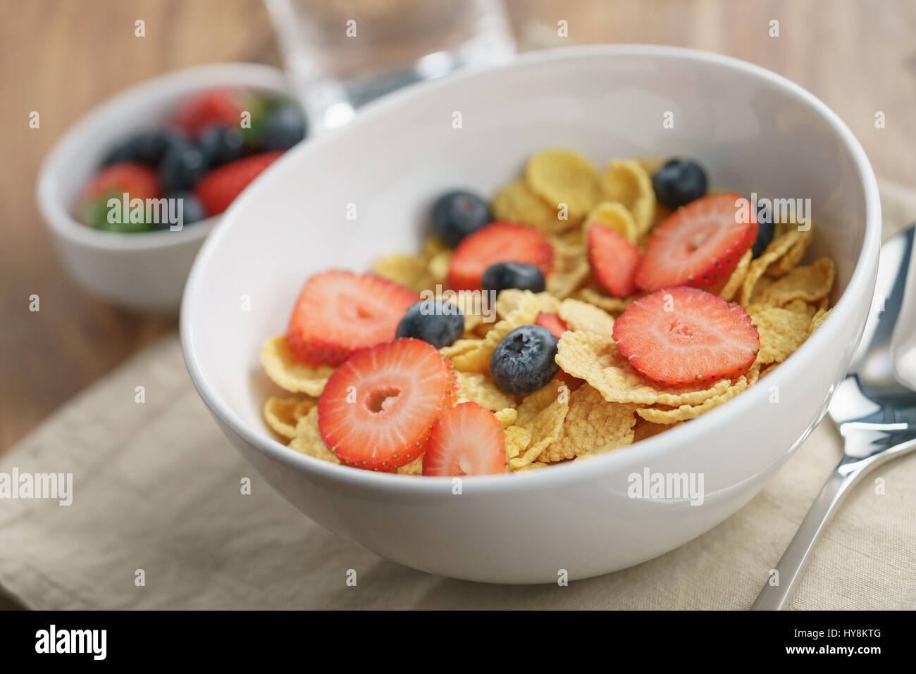 dry corn flakes with berries in bowl on table, breakfast preparation ...
