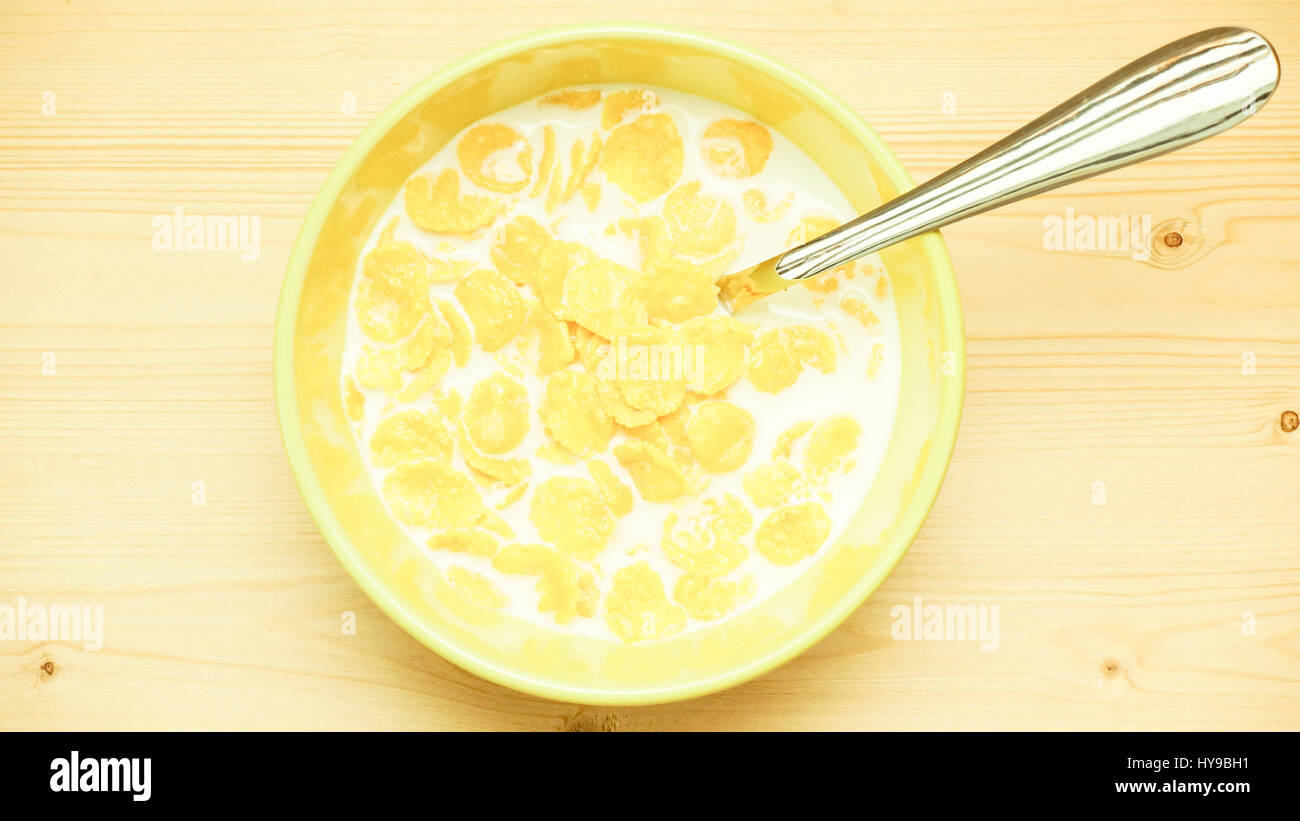 Ready corn flakes in a yellow bowl with a spoon on a wooden table, top ...