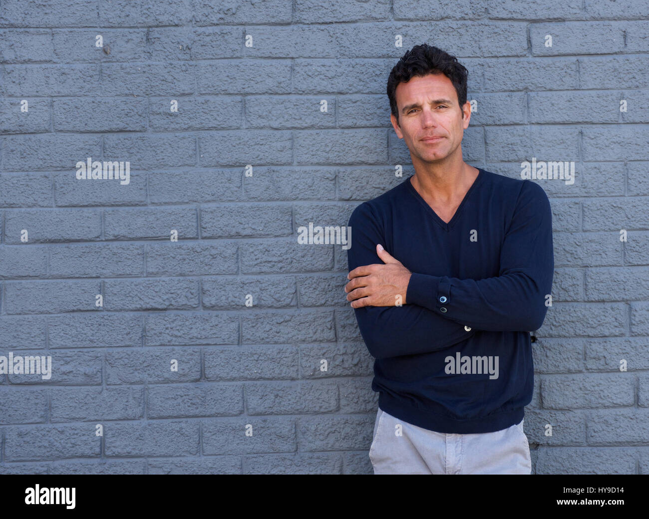 Portrait of a mature man standing against gray wall with arms crossed ...