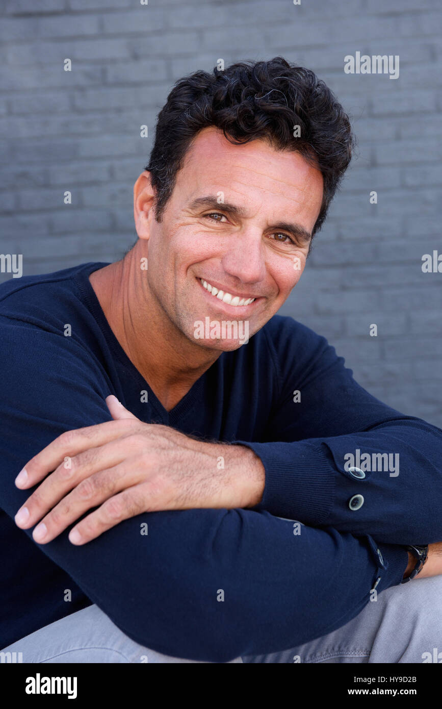 Close up portrait of older male fashion model sitting by gray wall ...