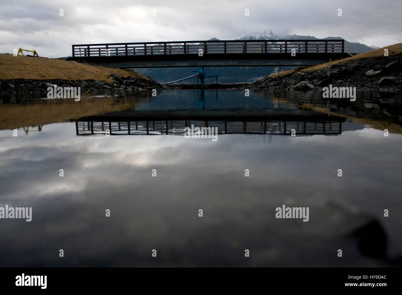 A small simple bridge is reflected in calm water with mountains in ...