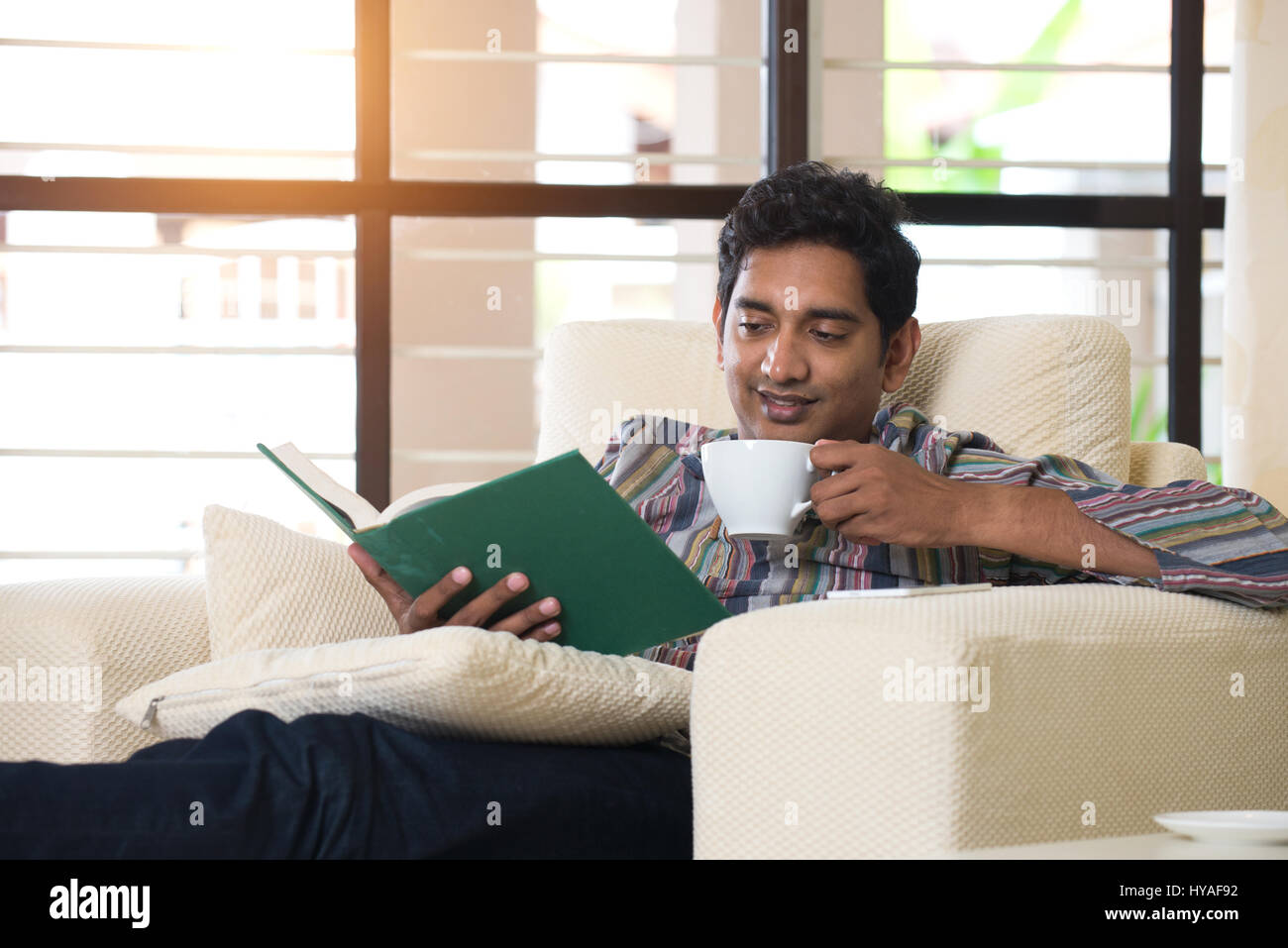 indian male reading book on sofa Stock Photo - Alamy