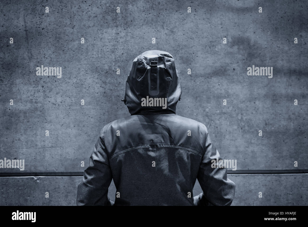 Unrecognizable hooded female person facing concrete wall as ...