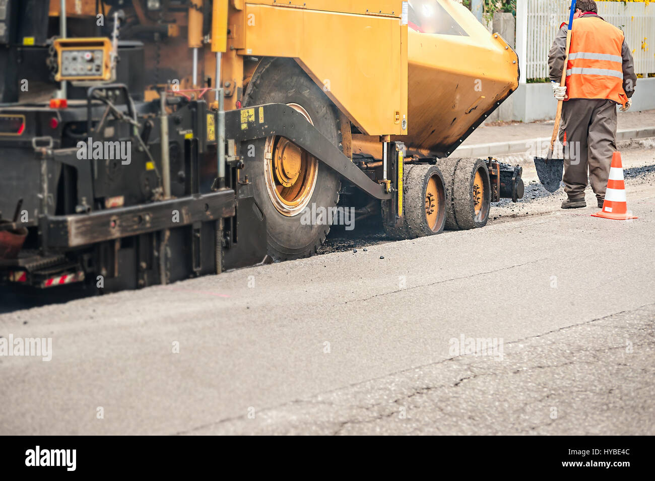 Worker with shovel checks the work of asphalt pavement machine ...