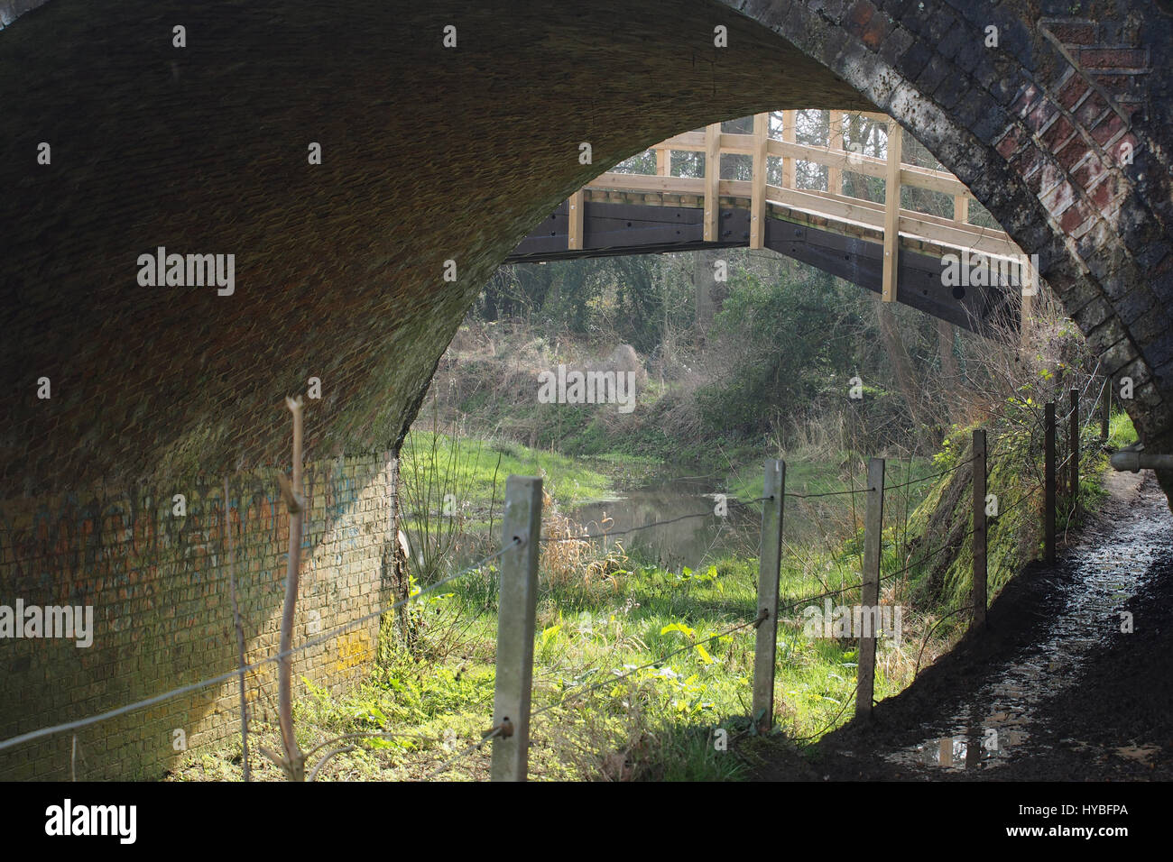 View through a railway arch to a wooden footbridge in the countryside ...