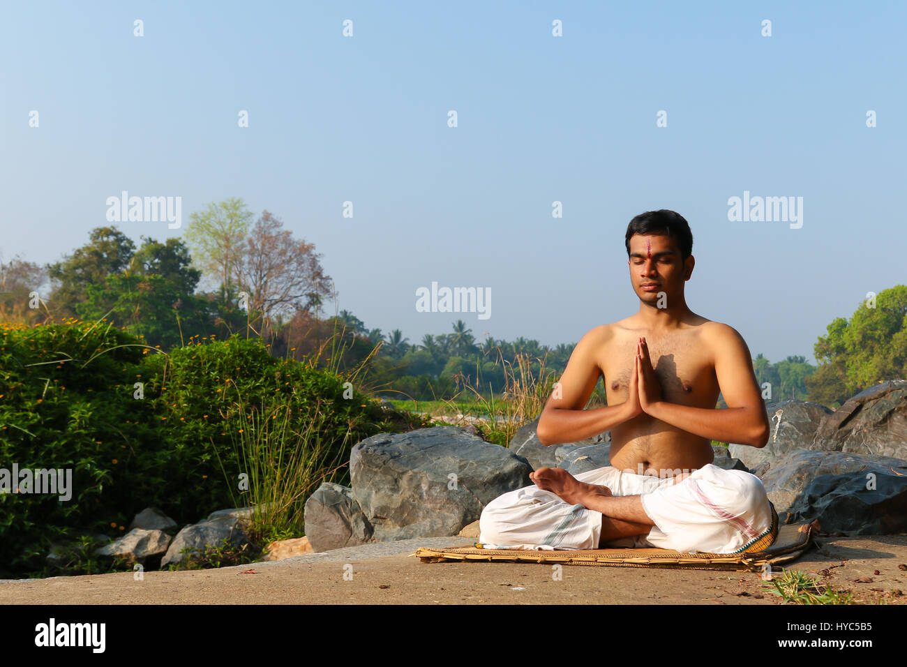 Indian man practicing yoga meditation next to a river in South India ...