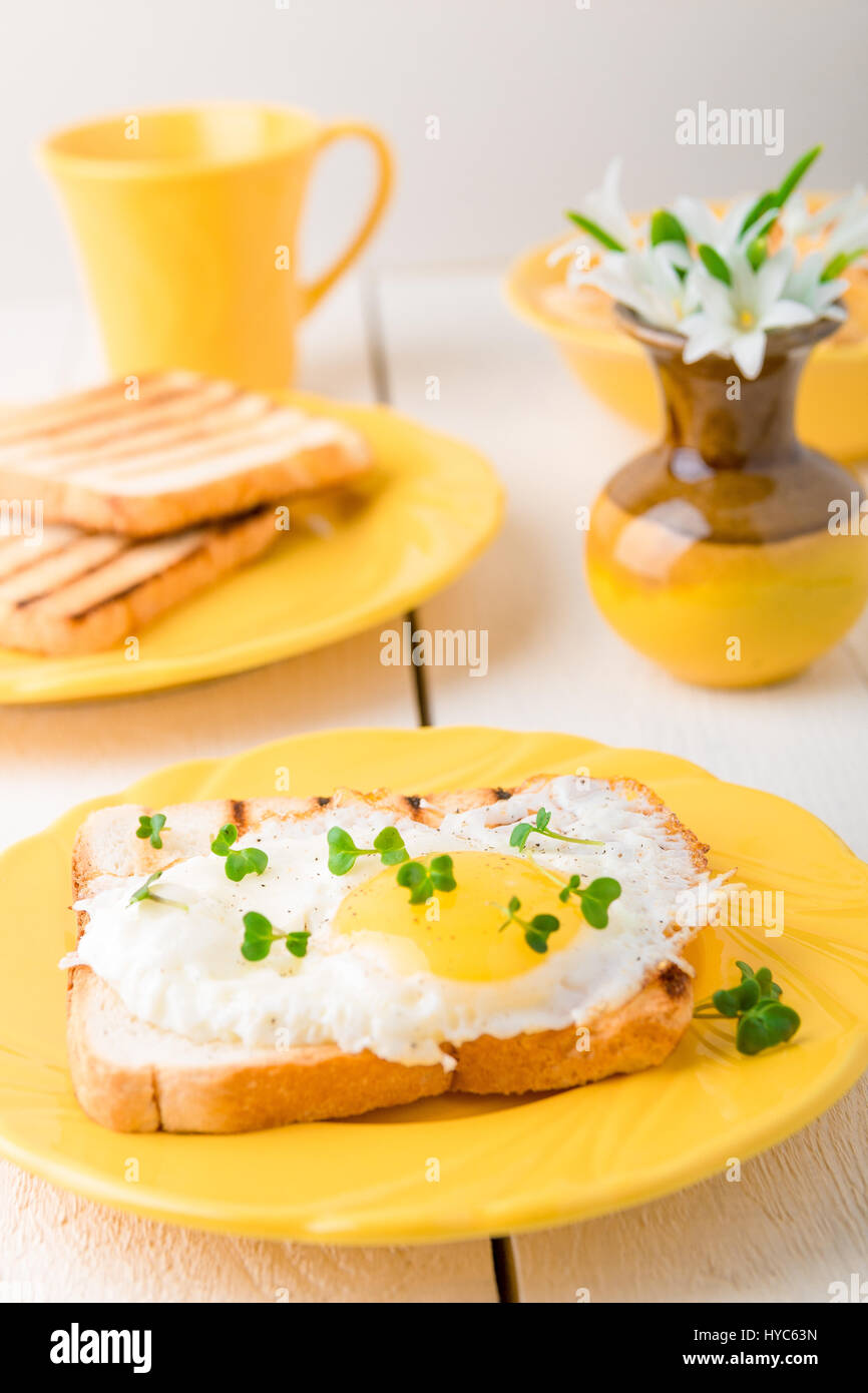 Toast with egg in yellow plate near vase with flower on white wooden ...