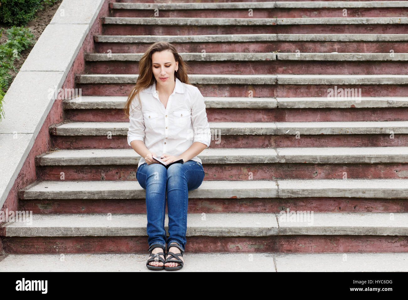 Young caucasian girl sitting on stairs with notebook. Thoughtful woman ...